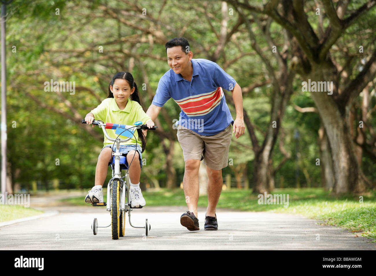 Girl cycling, father running behind her Stock Photo - Alamy