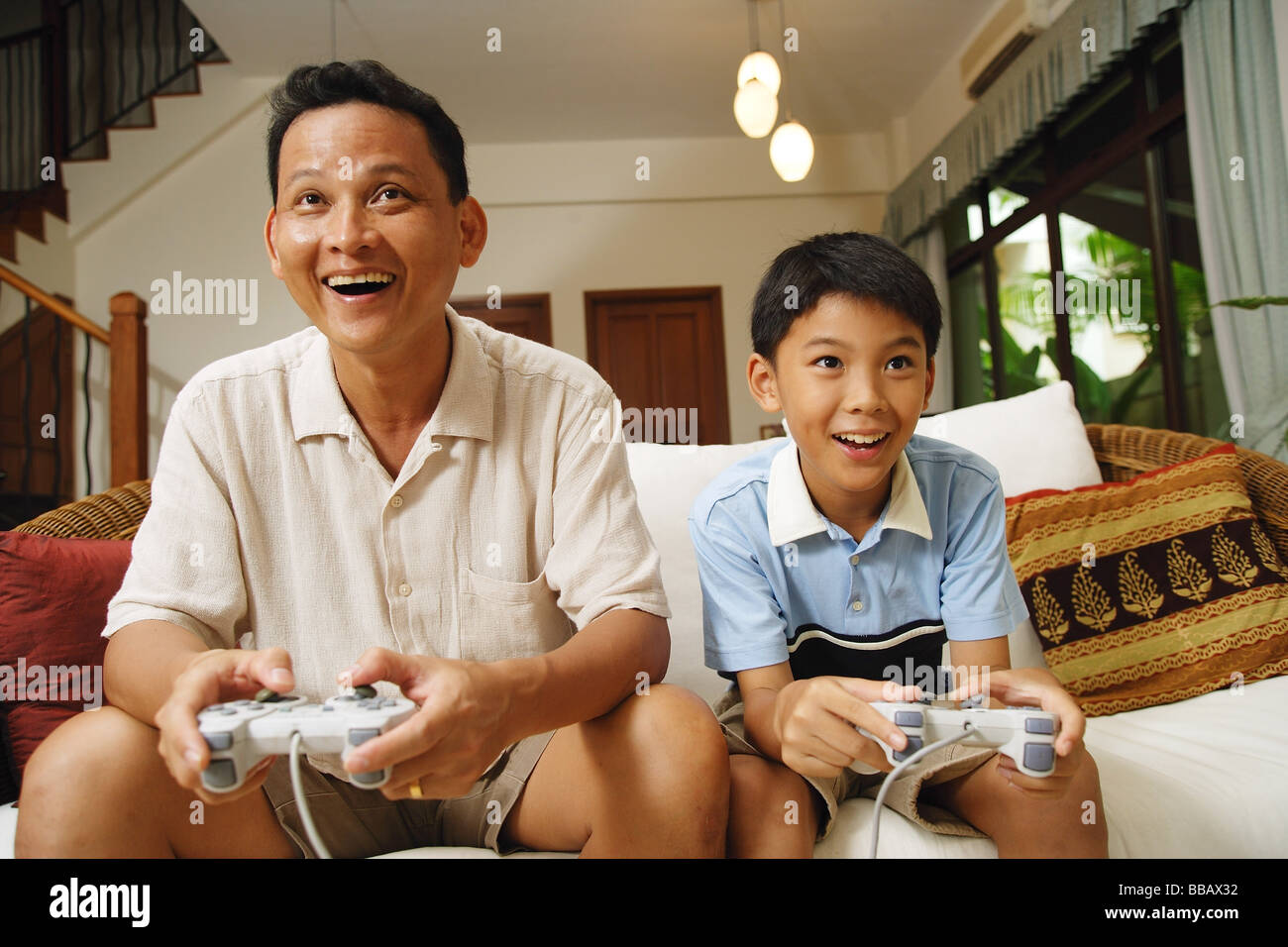 Father and son, sitting on sofa, holding video game controllers Stock ...