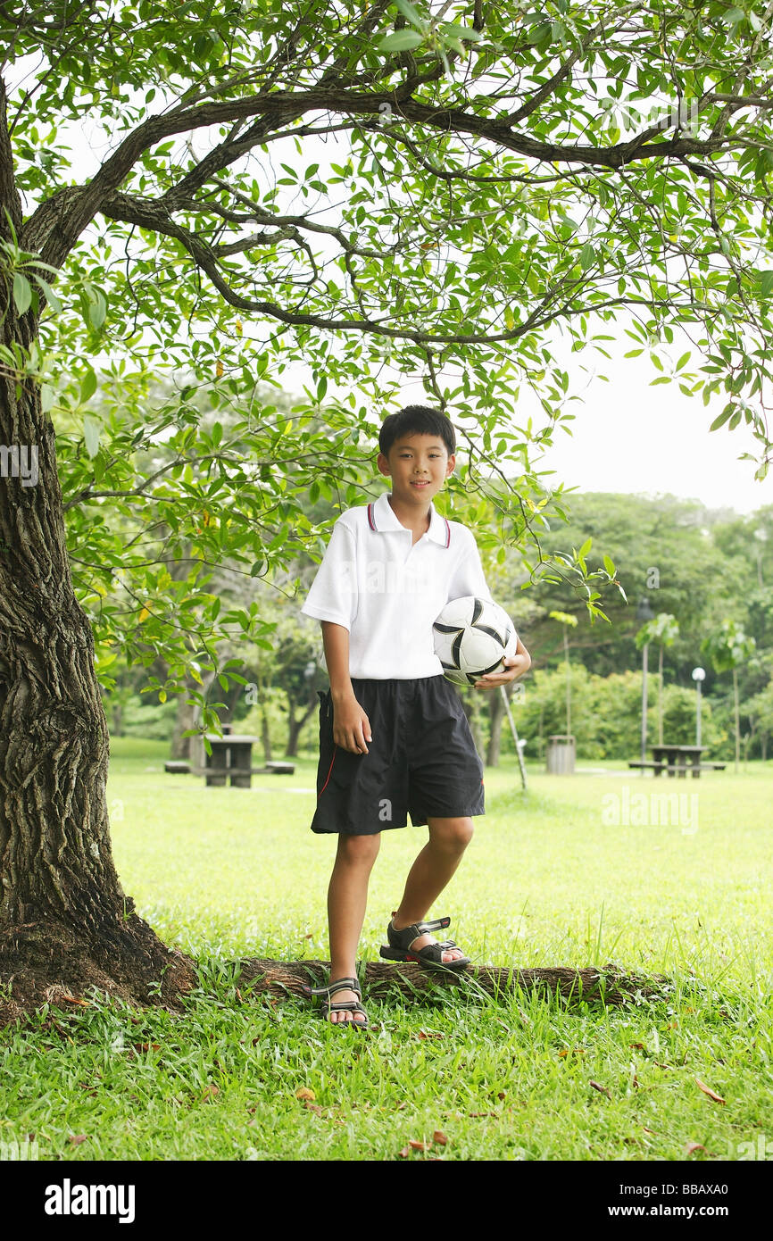 Boy holding ball, standing under tree Stock Photo - Alamy