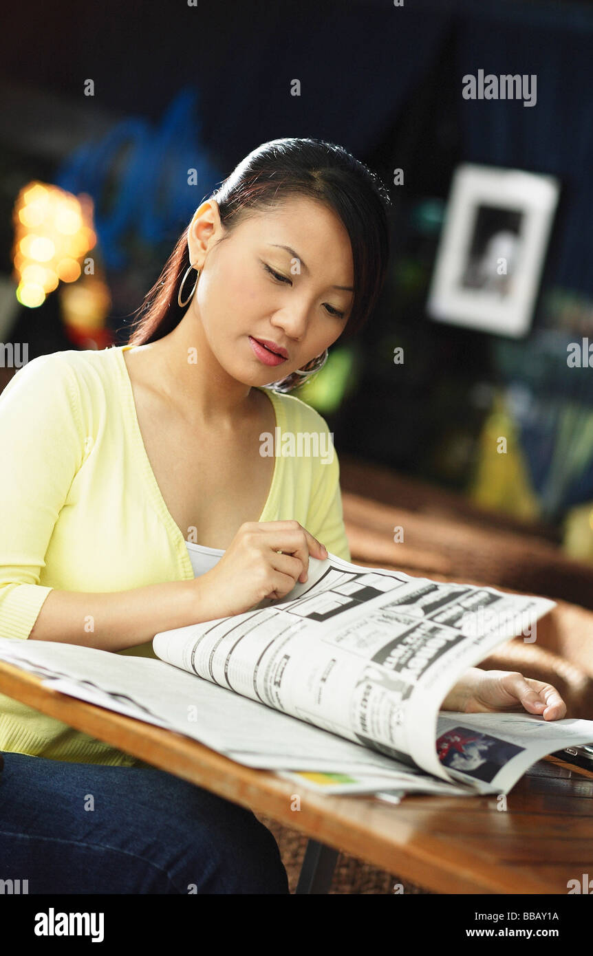 Young woman sitting at table, reading newspaper Stock Photo - Alamy
