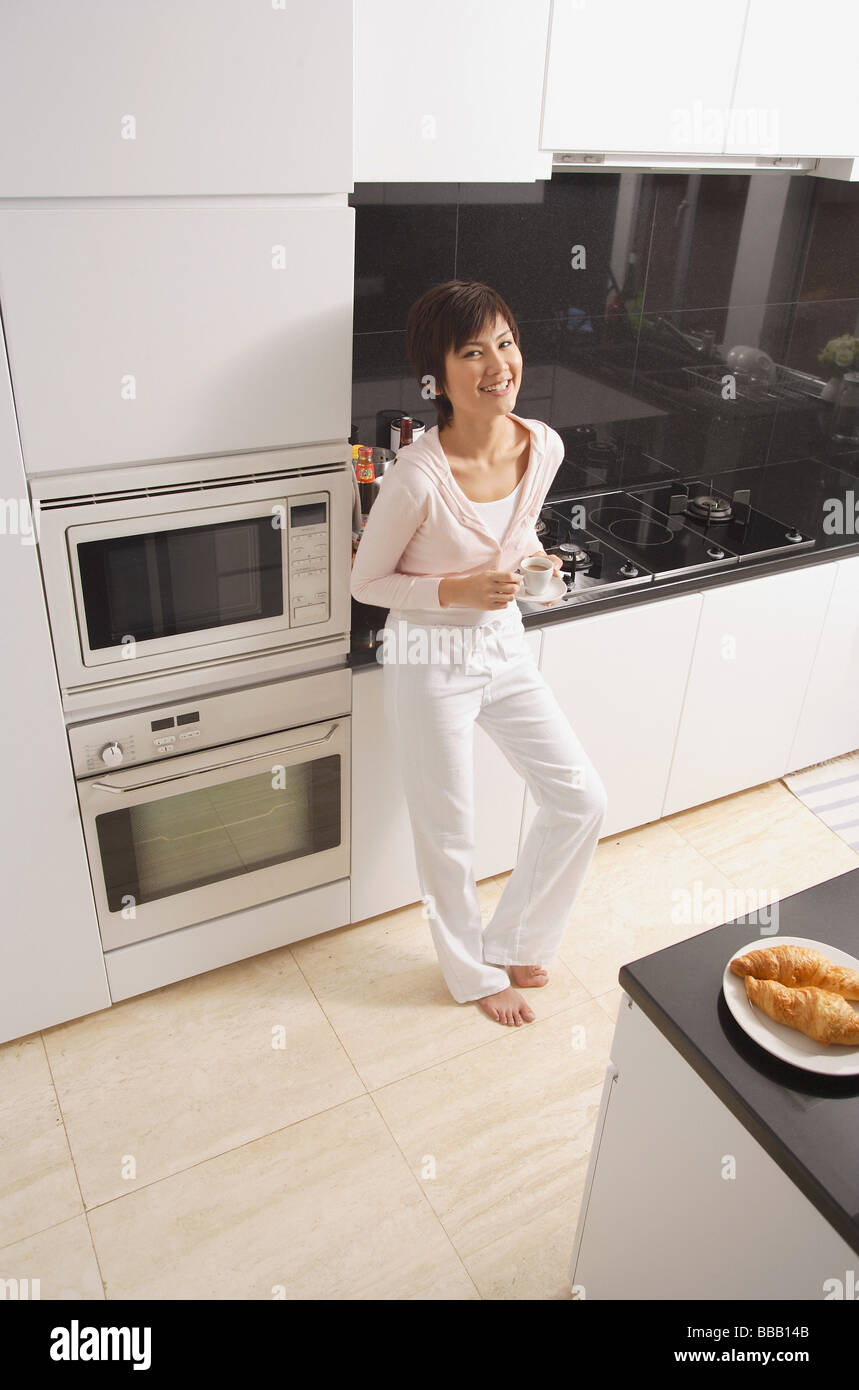 Young woman standing in kitchen, looking at camera, smiling Stock Photo ...