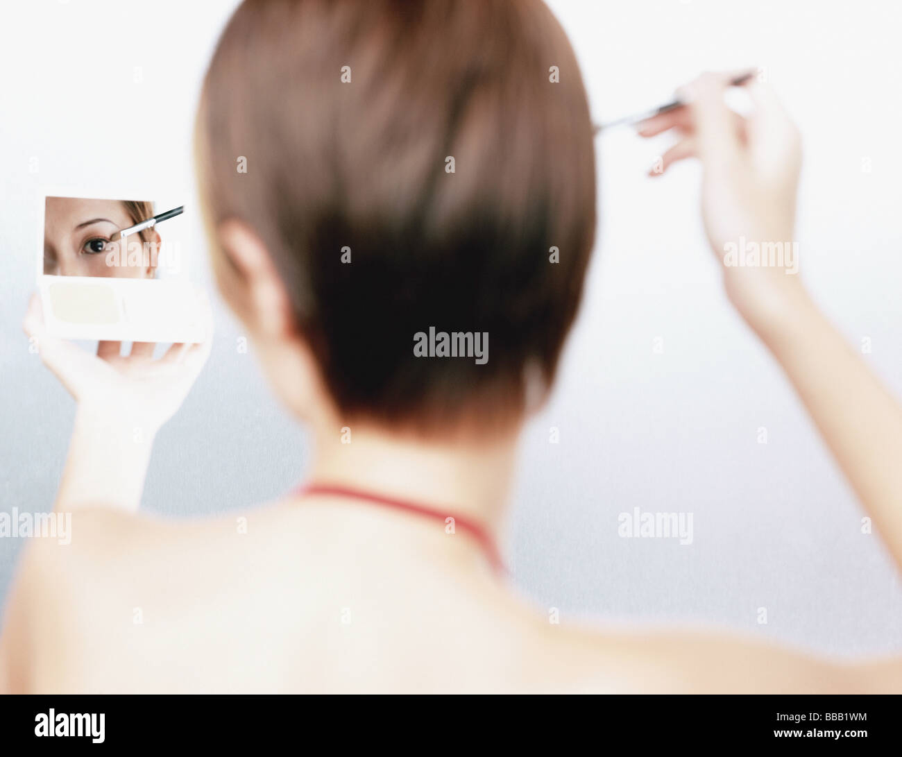Woman applying make-up, looking in compact mirror, rear view Stock ...