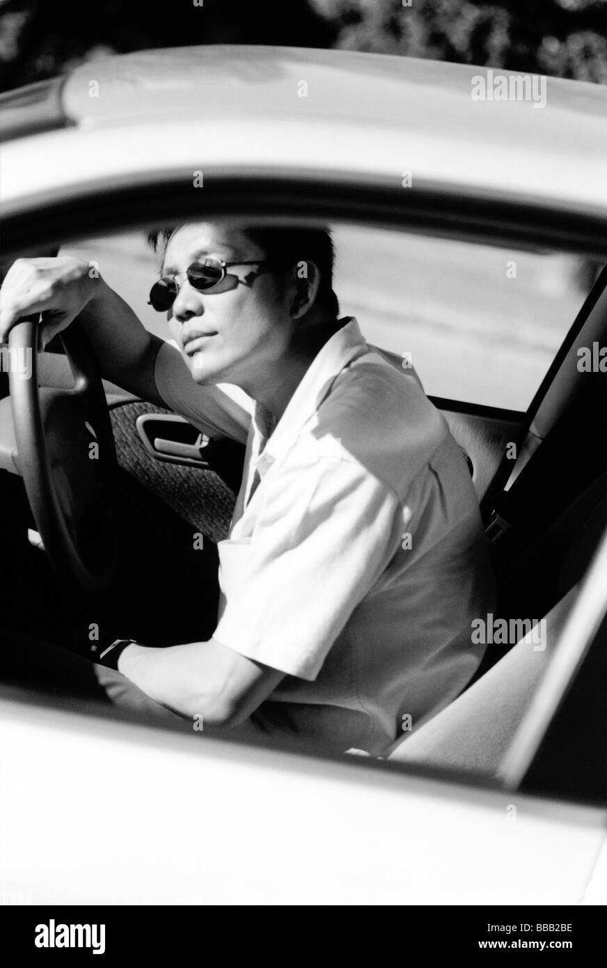 Male driver wearing sunglasses leaning forward in car to look out the ...