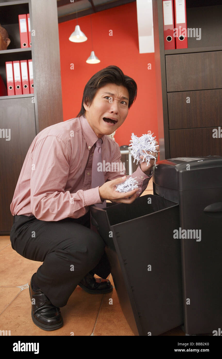 Executive next to paper shredder, holding shredded paper, making a face ...
