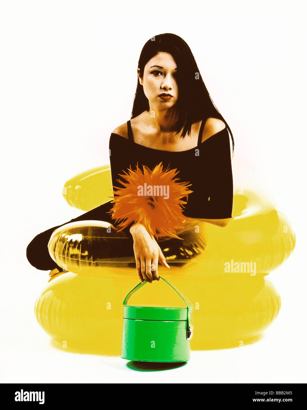 Young woman sitting on yellow inflatable chair, holding green purse ...