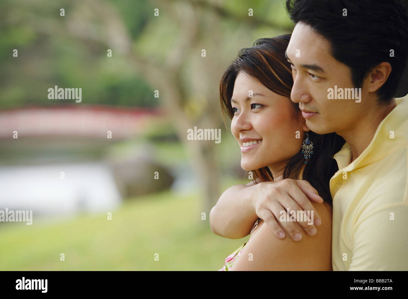 Man embracing woman from behind, arm around her shoulder, both looking ...