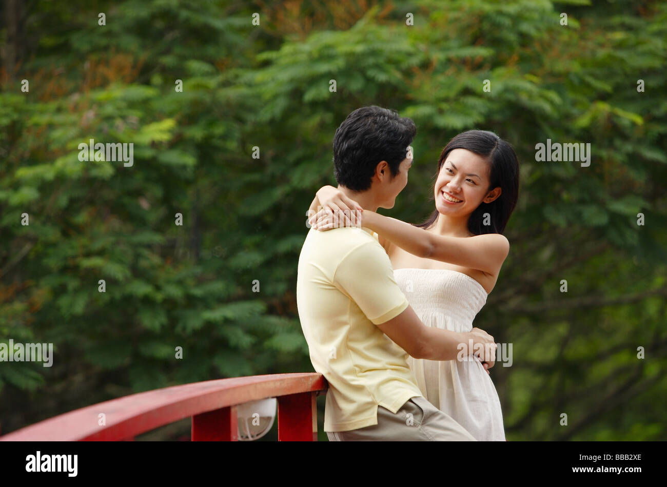 Couple standing face to face on bridge, woman with arms around mans ...