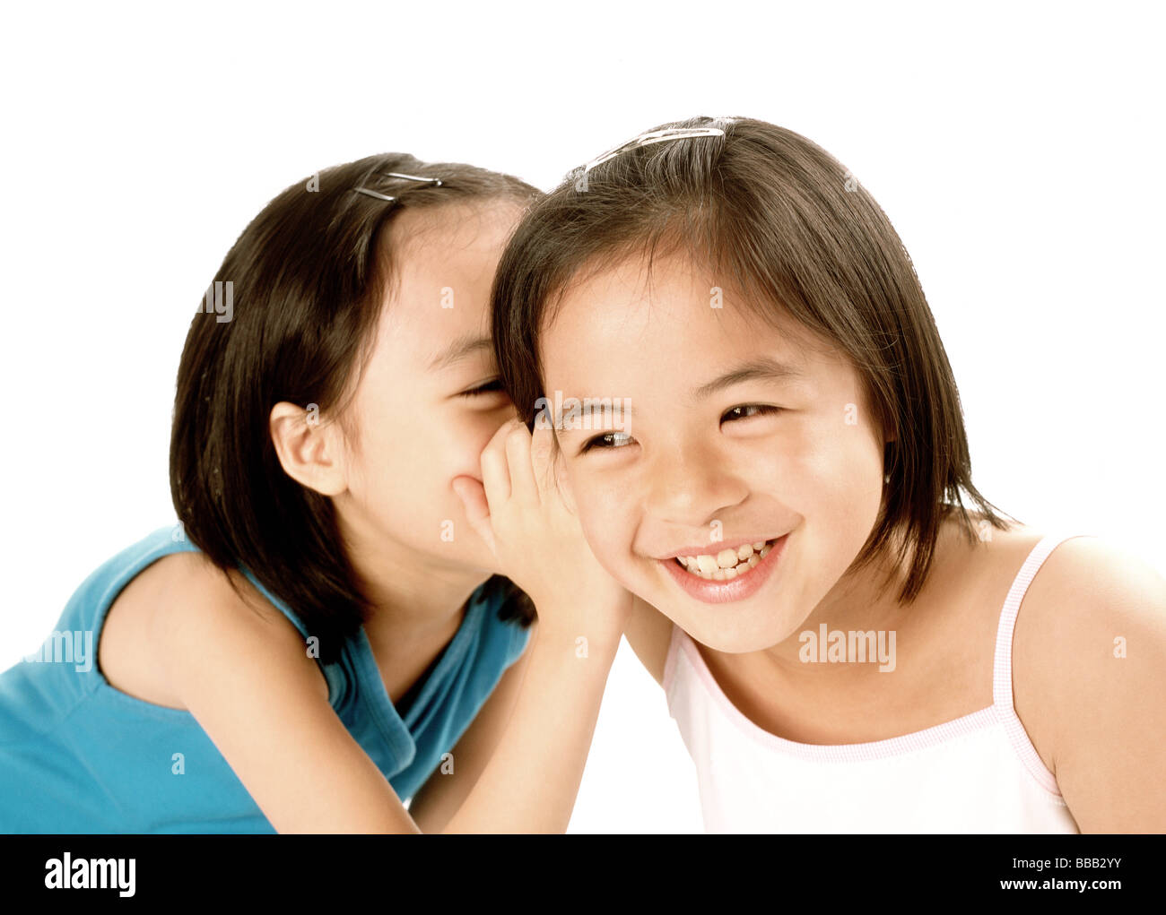 Two young girls whispering to each other, laughing, white background ...