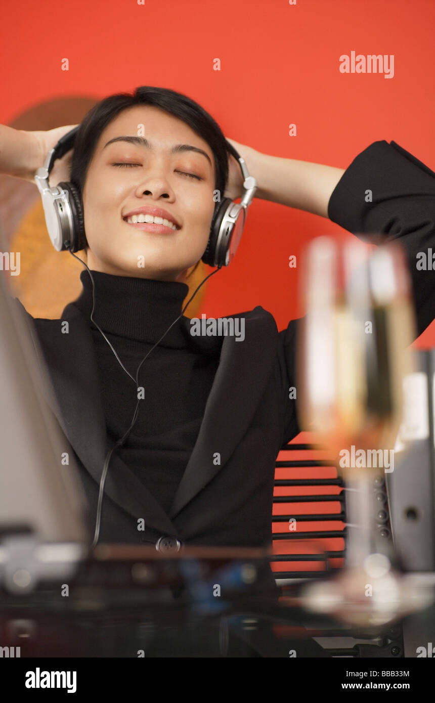 Female executive sitting at desk, listening to headphones, eyes closed ...