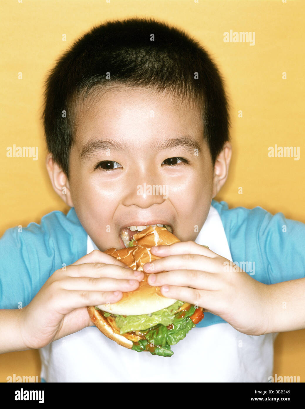 Young boy eating large hamburger, yellow background Stock Photo - Alamy