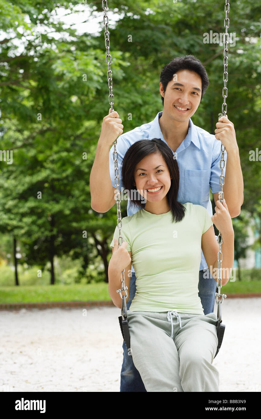 Woman sitting on swing, man behind her, smiling at camera Stock Photo ...