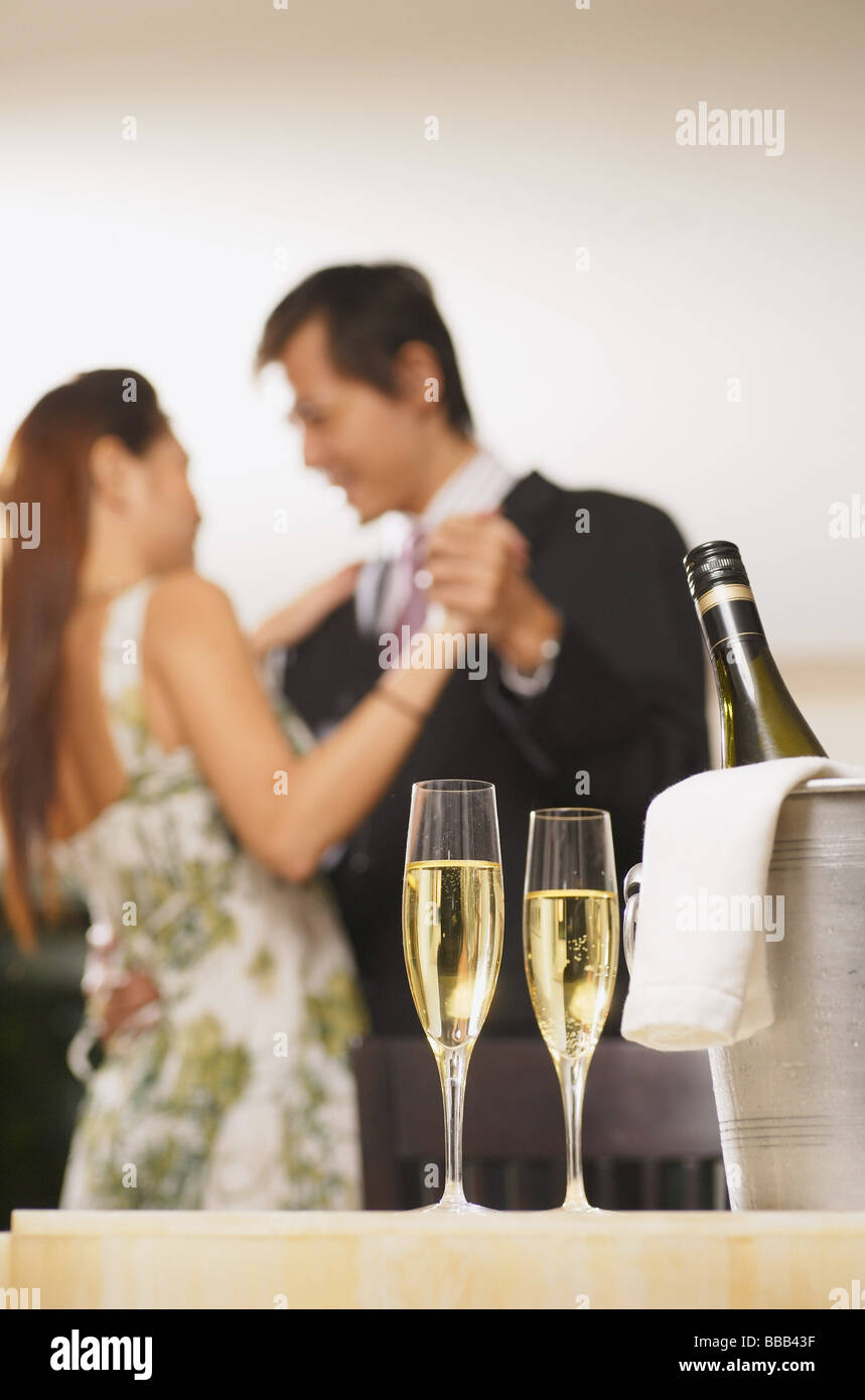 Champagne glasses and bottle in foreground, couple dancing in ...