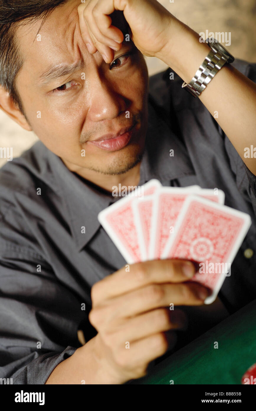 Gambler holding cards, looking worried Stock Photo - Alamy