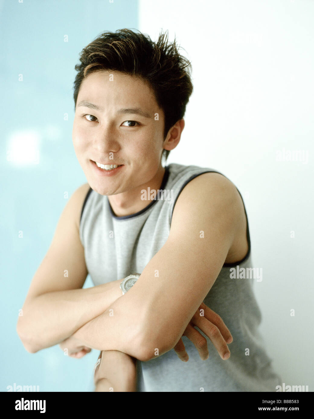 Young man leaning against rail smiling, blue/white background, portrait ...