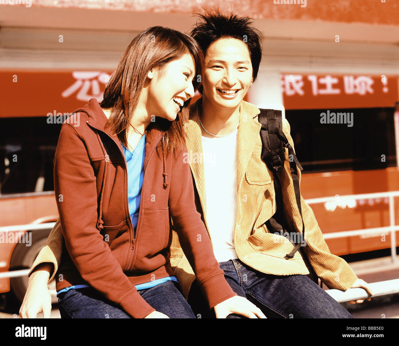 Young woman and man sitting together on rail Stock Photo - Alamy