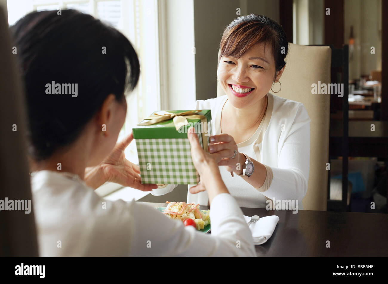 Woman giving gift to person sitting opposite her Stock Photo - Alamy