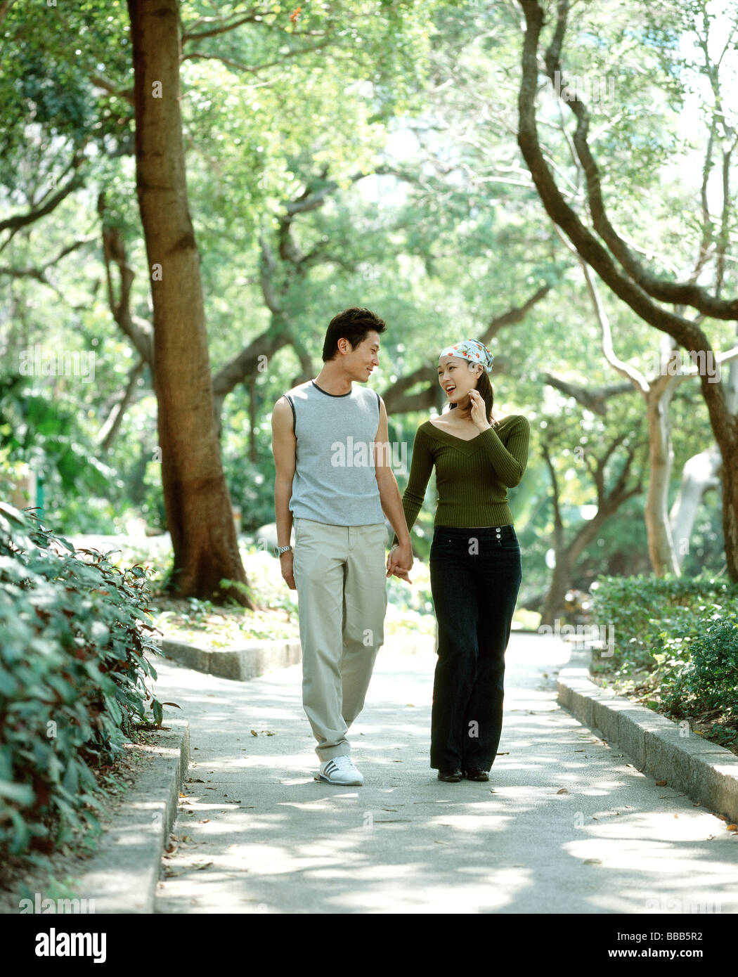 Young couple walking down path holding hands, nature in background ...