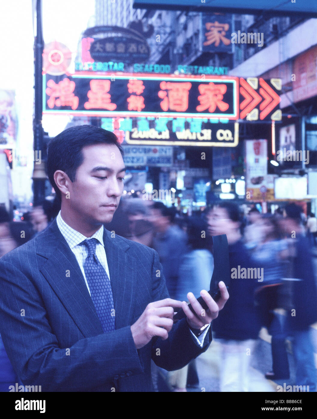 Male executive dialing cellular phone in busy street, neon lights in ...