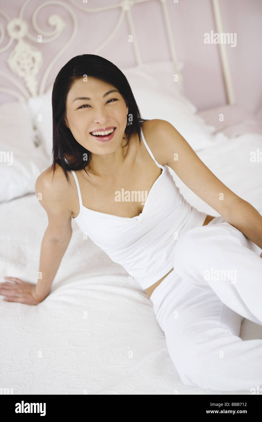 Woman sitting on bed, smiling at camera Stock Photo - Alamy