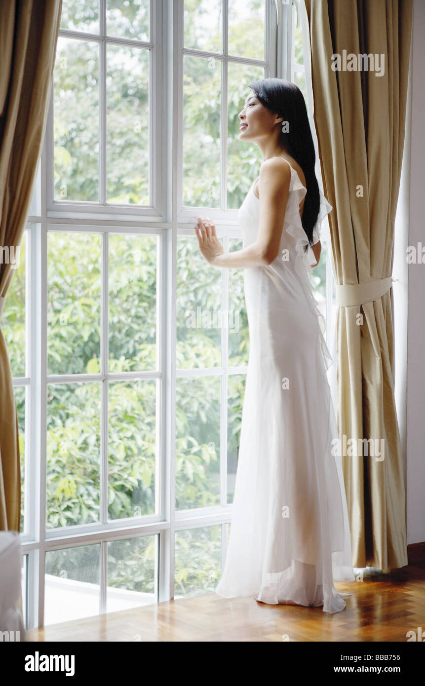 Woman standing by full length window, looking out Stock Photo - Alamy