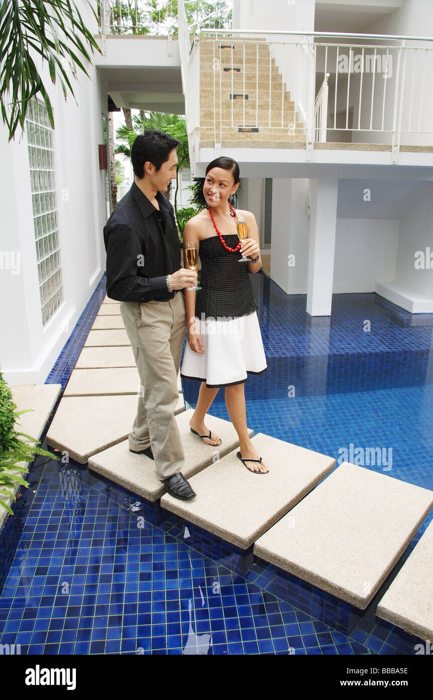 Couple walking by swimming pool, champagne glasses in hand Stock Photo ...