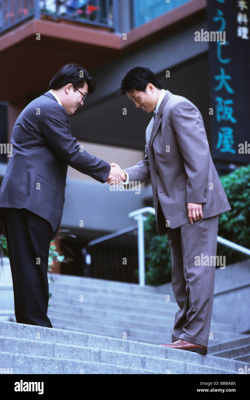 Two male executives bowing while shaking hands on stairway Stock Photo ...
