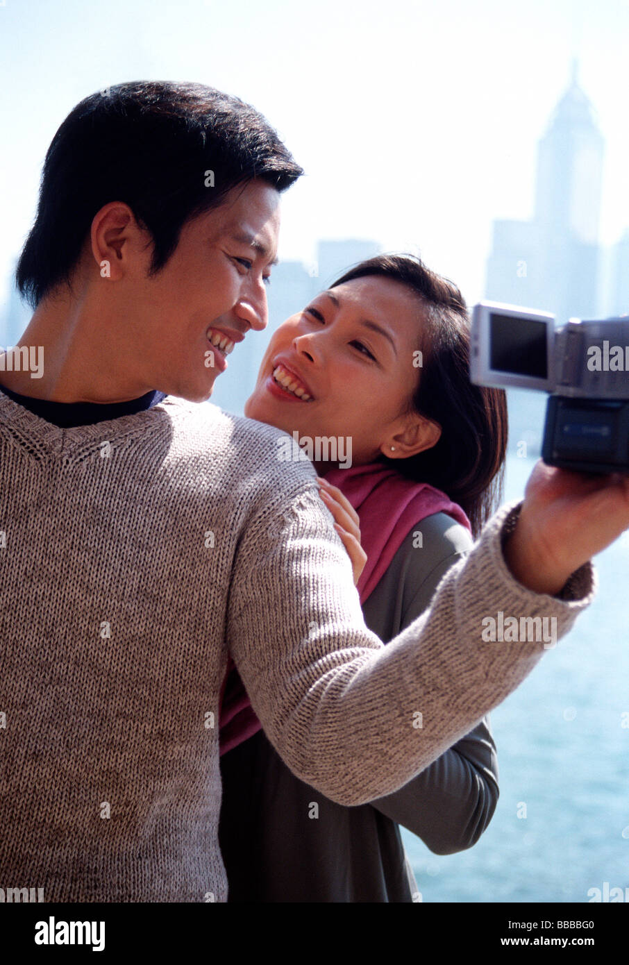 Couple looking at each other by waterfront, man holding video camera ...