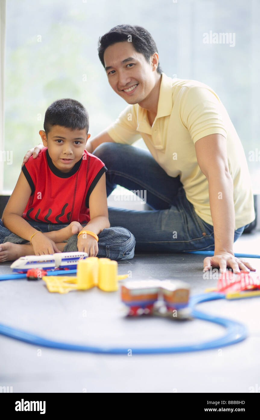 Father and son looking at camera, toy train set on floor in front of ...