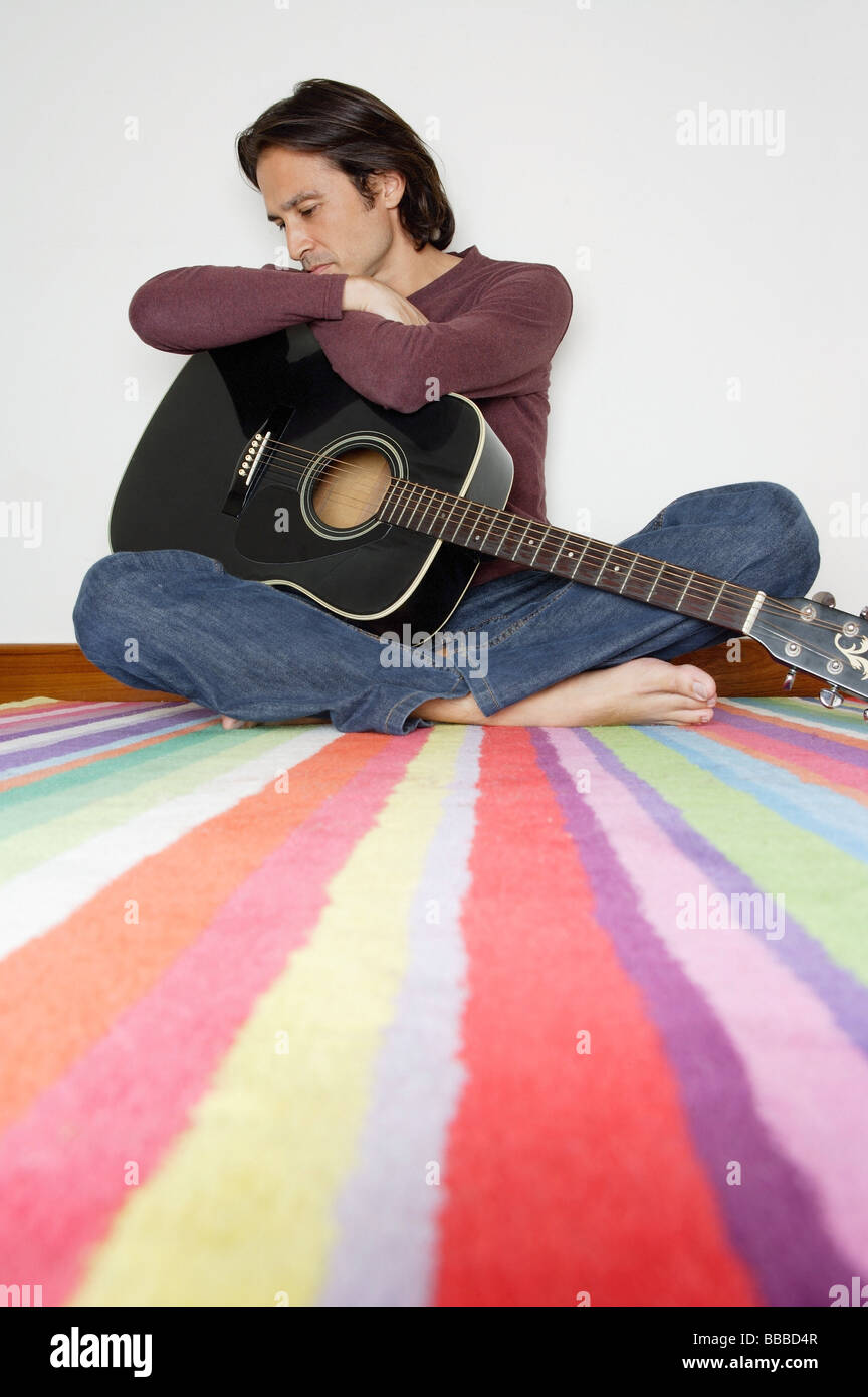 Man holding guitar, sitting cross-legged on floor, looking down Stock ...