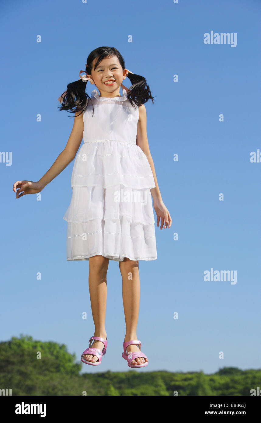 Girl wearing white dress, jumping in mid air, smiling at camera Stock ...