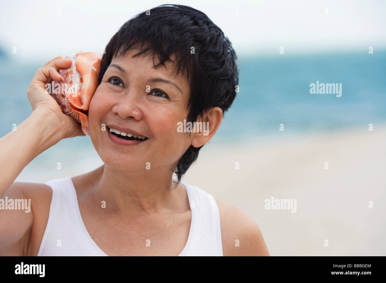 Woman at the beach listening to sea shell Stock Photo - Alamy