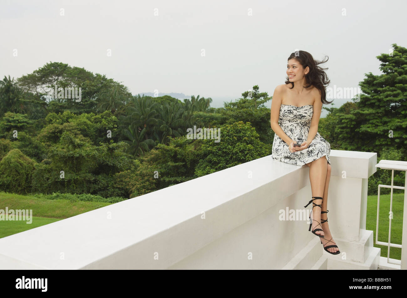 Young woman sitting on balcony ledge, looking away Stock Photo - Alamy