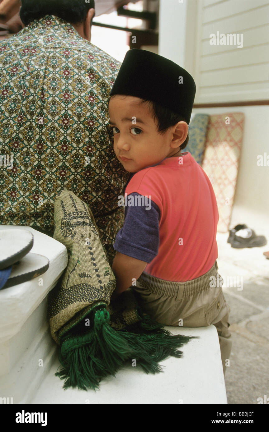 Malaysia, Malacca, Muslim boy with prayer rug nestles besides his ...