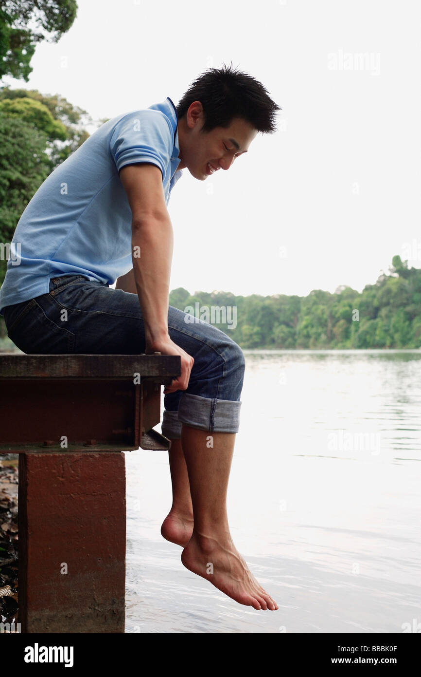 Man sitting on jetty, looking down at water Stock Photo - Alamy