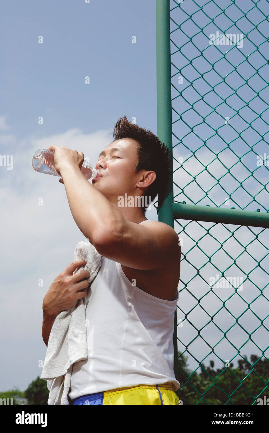 Man leaning on fence, drinking from mineral water bottle Stock Photo ...