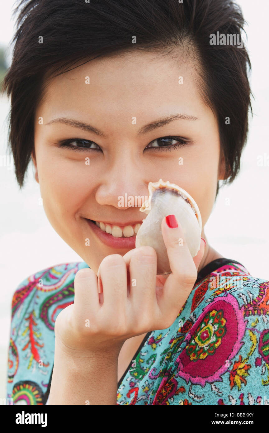 Woman holding shell, smiling at camera, portrait Stock Photo - Alamy