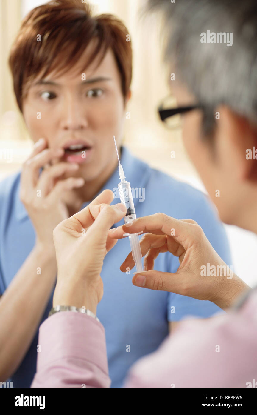 Doctor preparing syringe, patient cringing in background, selective ...
