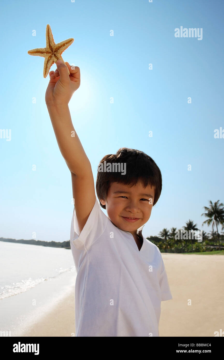 Young boy holding up shell at the beach, looking at camera Stock Photo ...