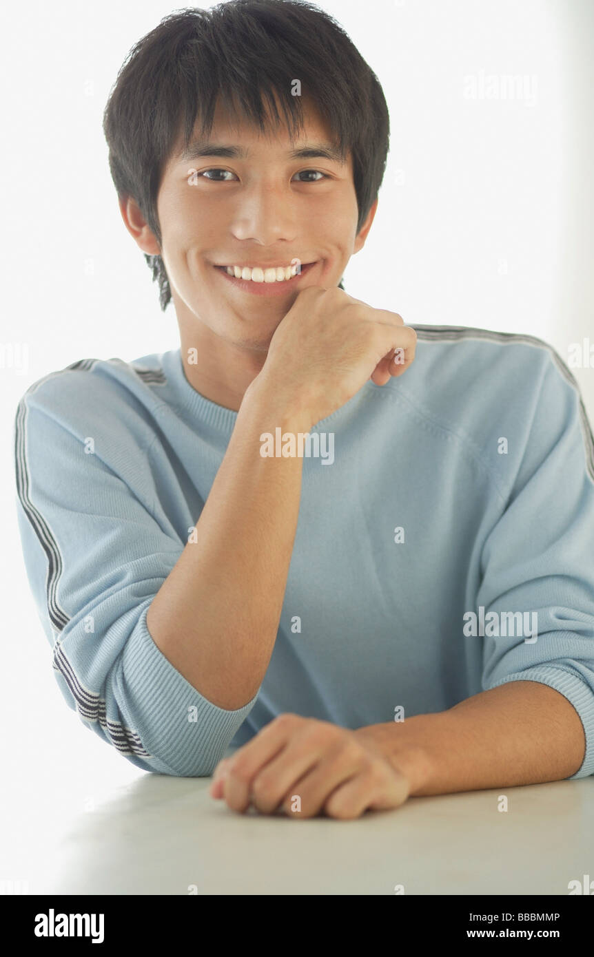 Young man sitting at table, smiling at camera, hand on chin Stock Photo ...