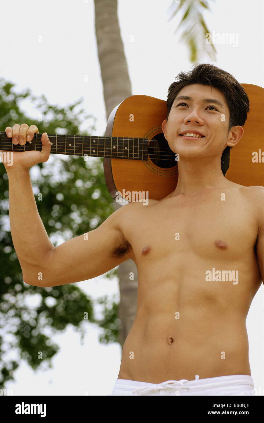 Young man standing, carrying guitar on shoulder Stock Photo - Alamy