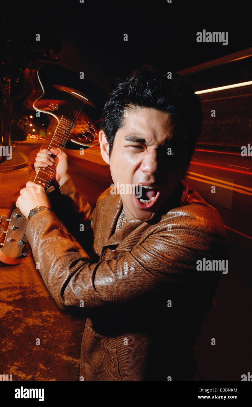 Young man holding guitar, making face Stock Photo - Alamy