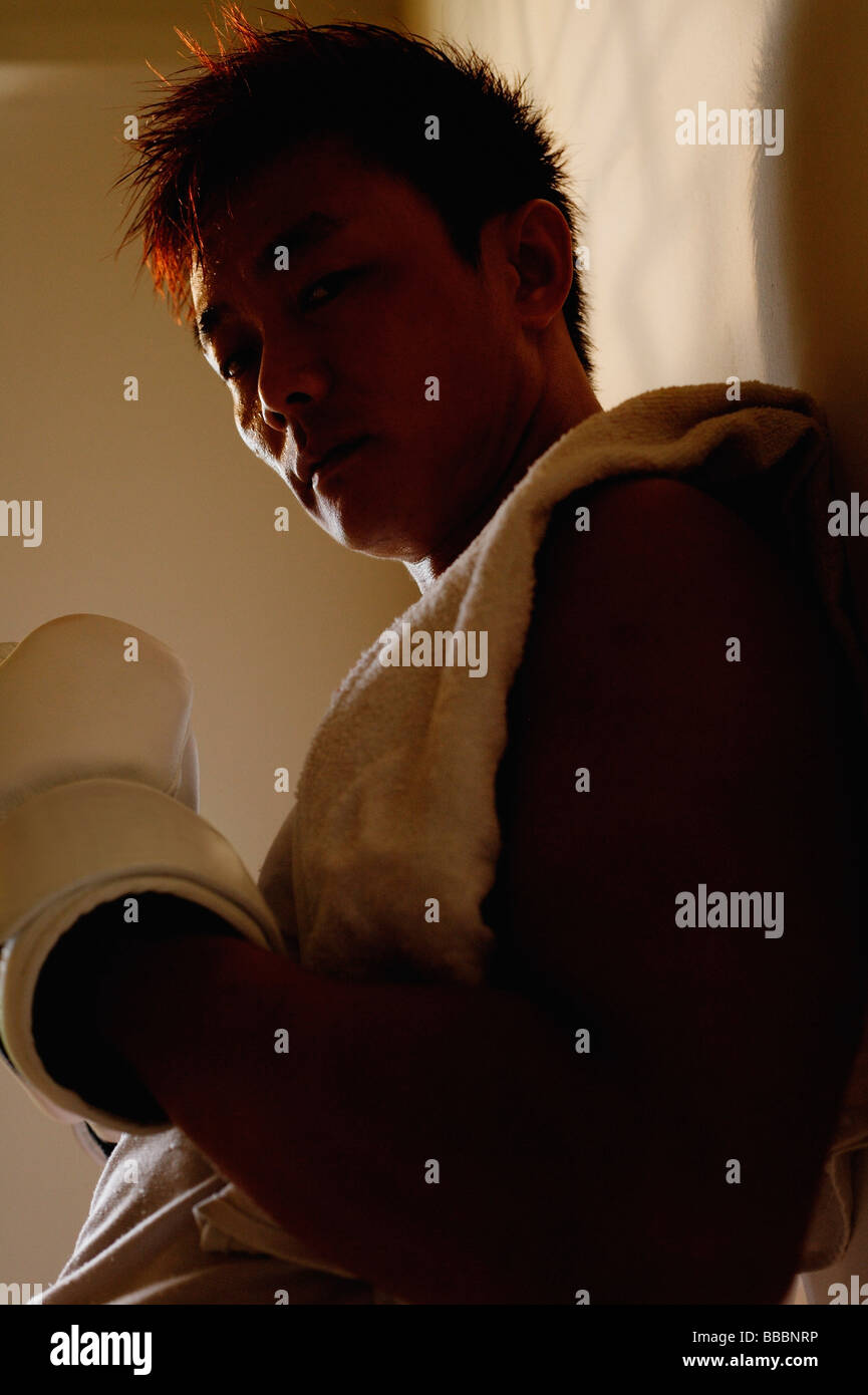 Man leaning on wall, boxing gloves on hand, looking down Stock Photo ...