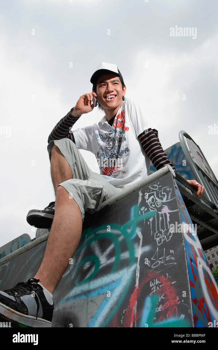 Young man using mobile phone, sitting on graffiti covered ledge Stock ...