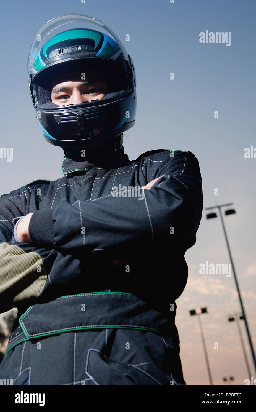 Race car driver in protective sportswear, arms crossed, looking at ...