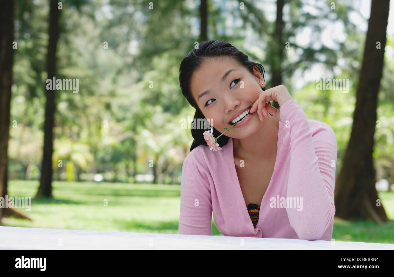 Young woman biting flower stalk, sitting outdoors Stock Photo - Alamy