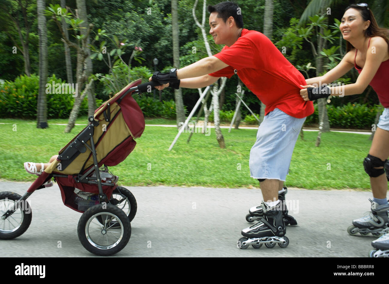 Father skating and pushing stroller, mother holding on to waist Stock ...