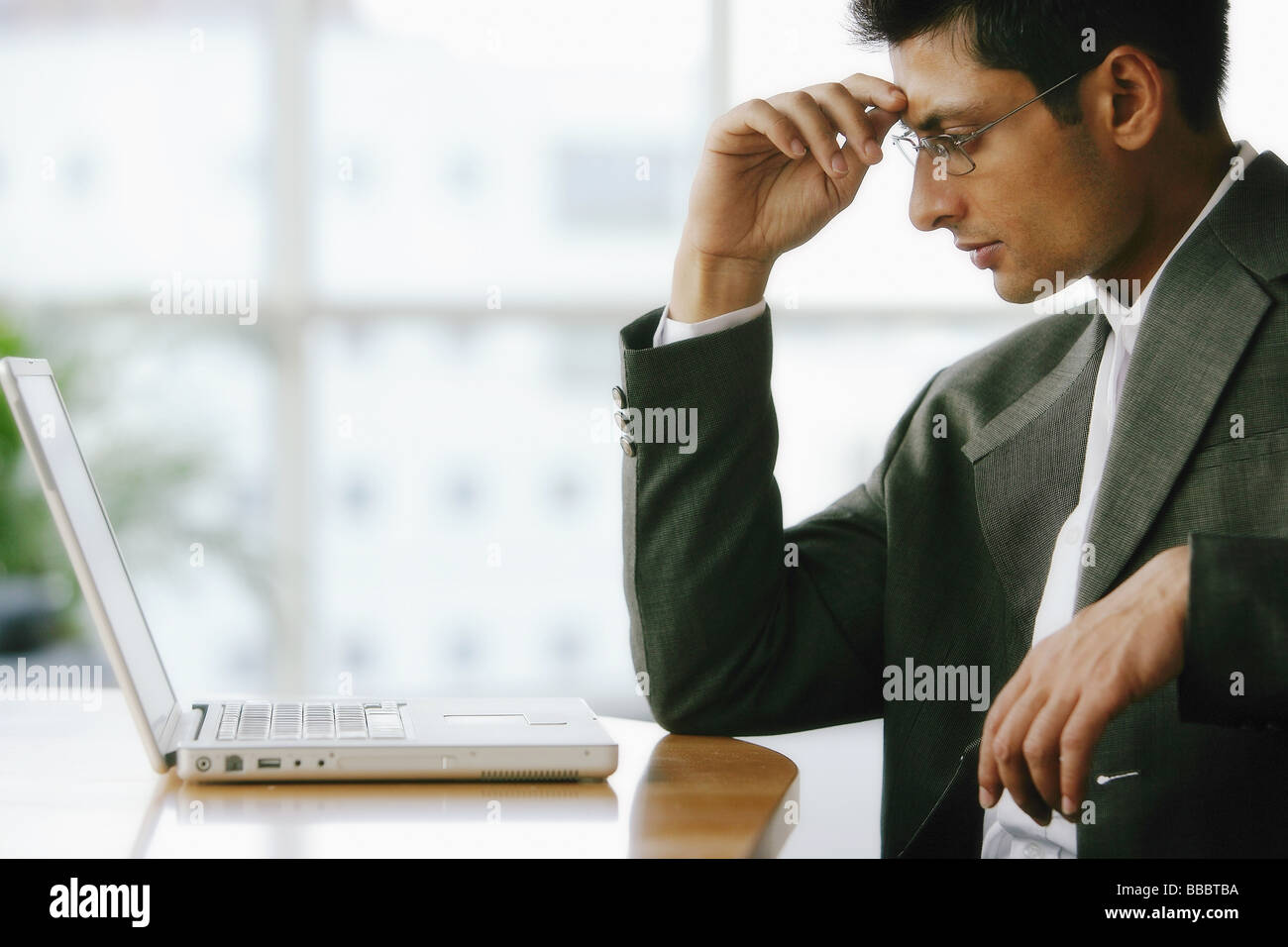 Man using laptop, hand on head, looking down Stock Photo - Alamy