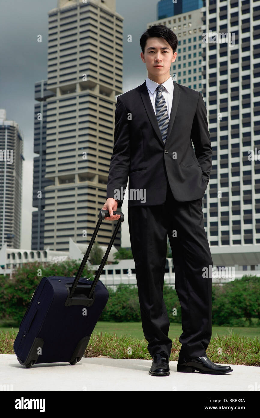 Businessman pulling luggage, looking at camera Stock Photo - Alamy