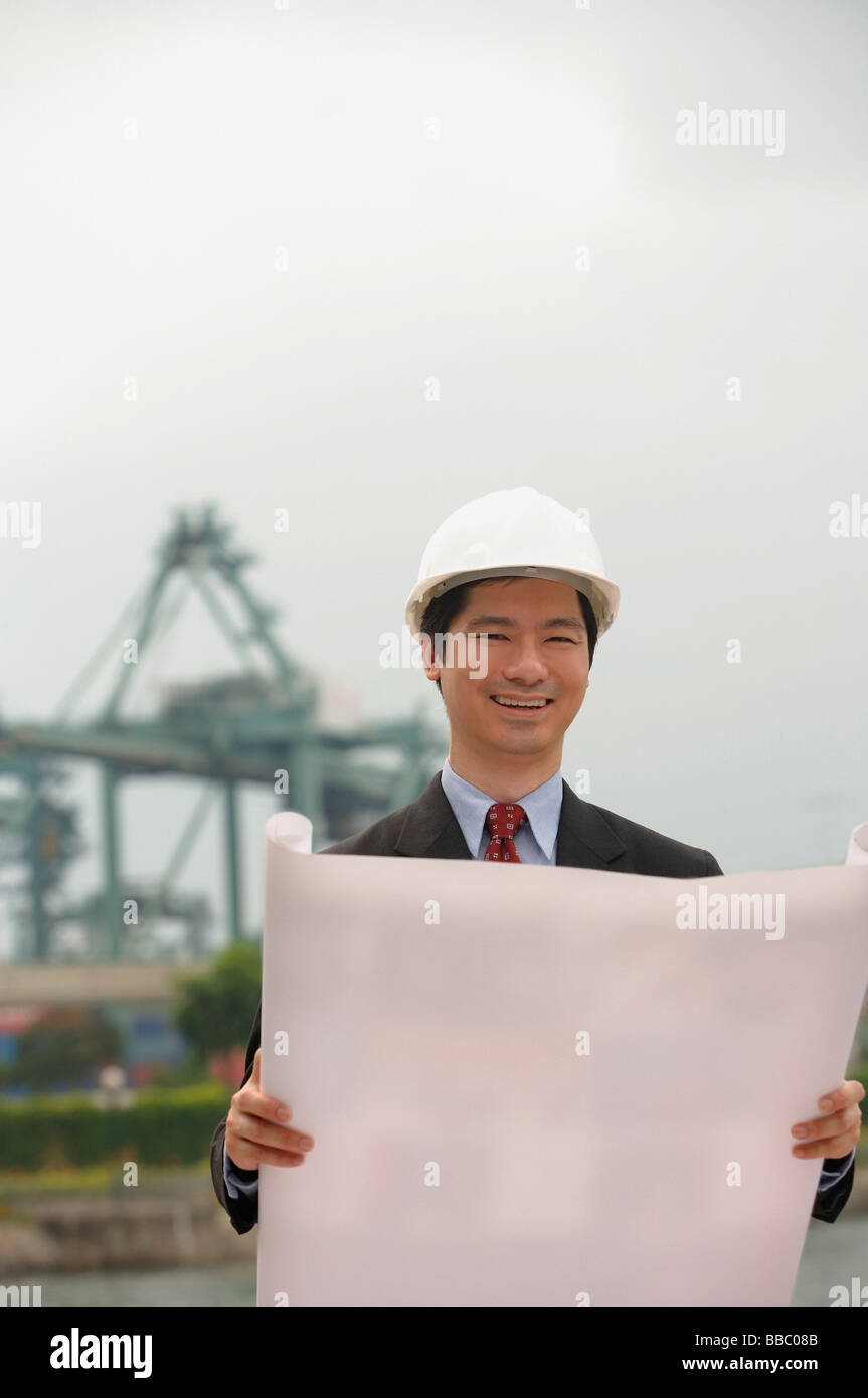 Engineer with plans and hard helmet looking at camera Stock Photo - Alamy