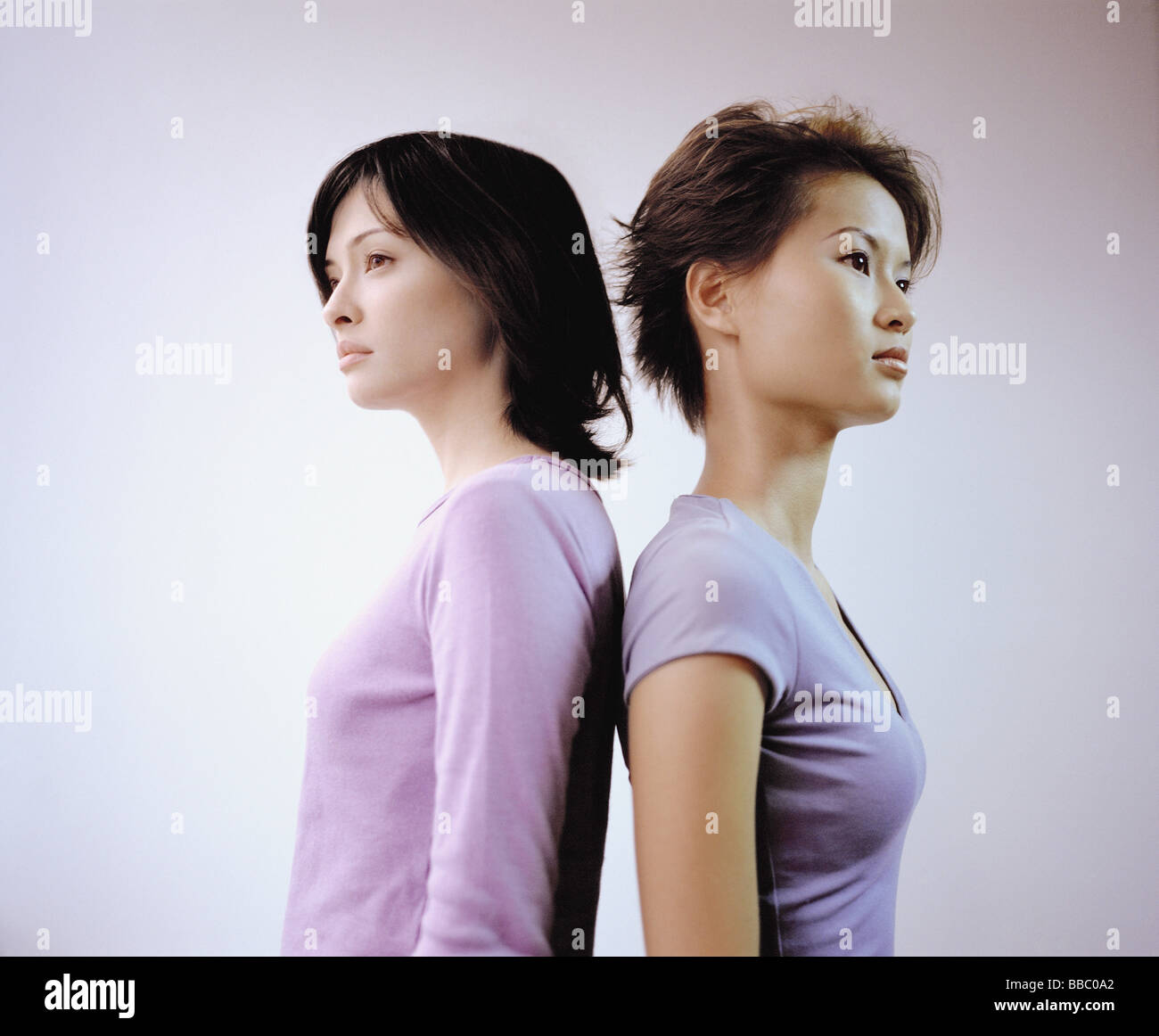 Two young women standing back to back, white background Stock Photo - Alamy